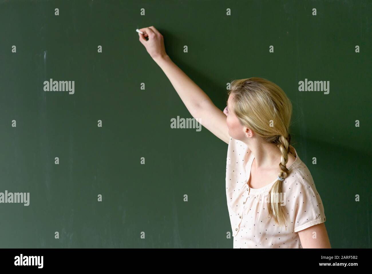 Female teacher with blond hair ponytail writing with chalk on top of a ...
