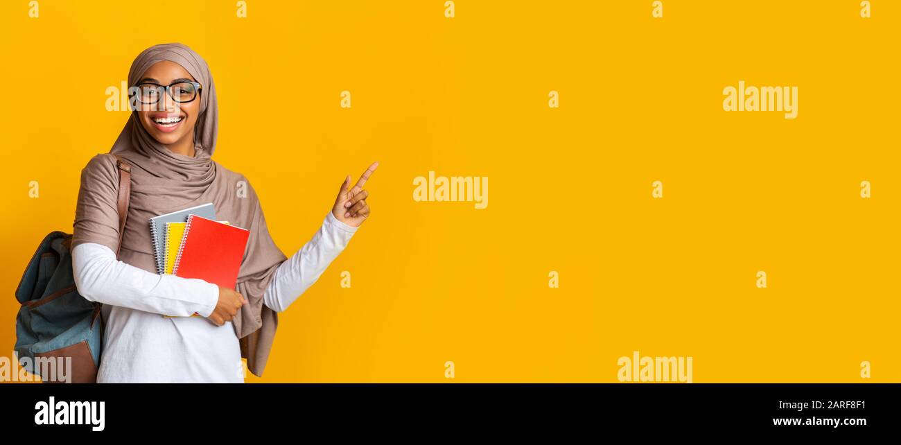 Portrait of black muslim female student in hijab pointing at copy space ...