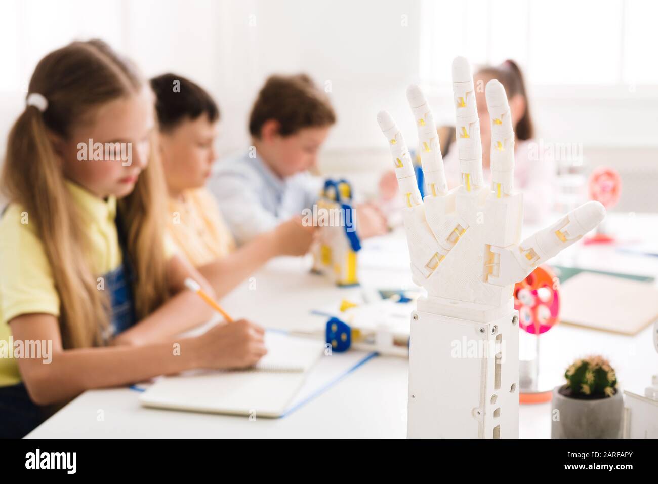 Children learning in class with humanoid robotic hand on foreground ...