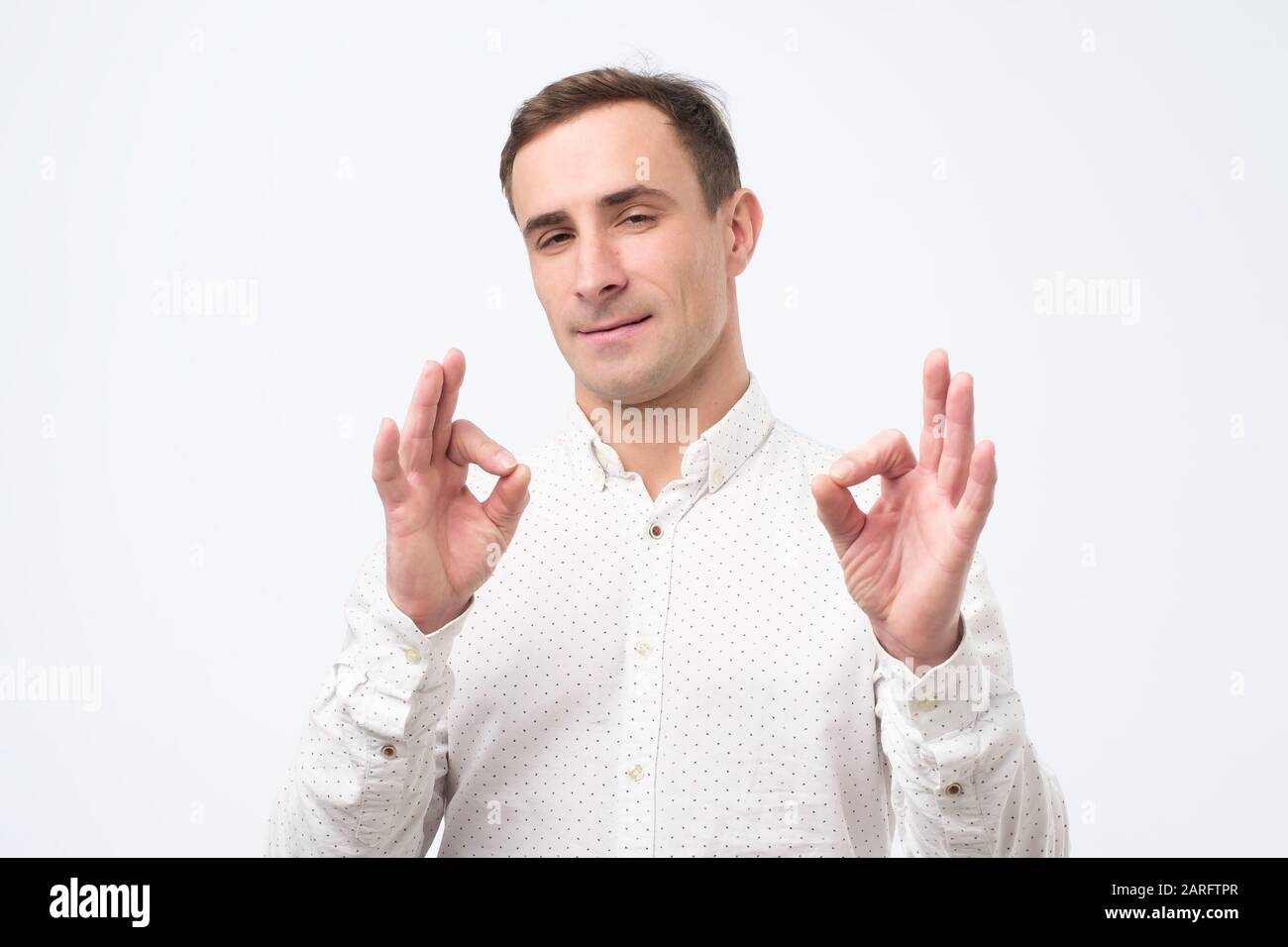 Portrait of cheerful italian young man in white shirt showing okay ...