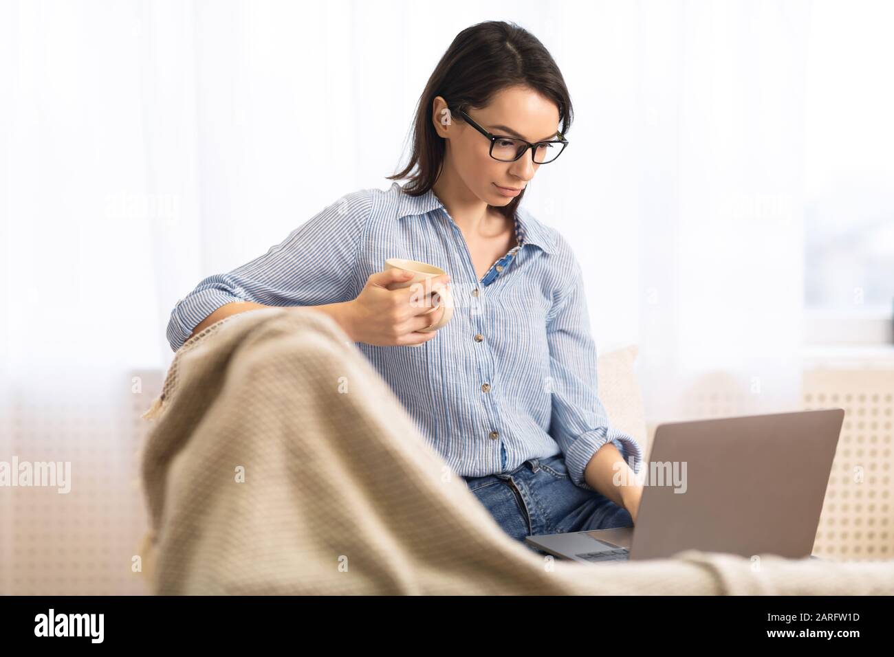 Young woman using laptop sitting on the sofa Stock Photo - Alamy
