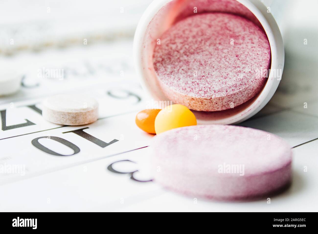 Large pink pills or vitamins near a jar on a calendar background ...