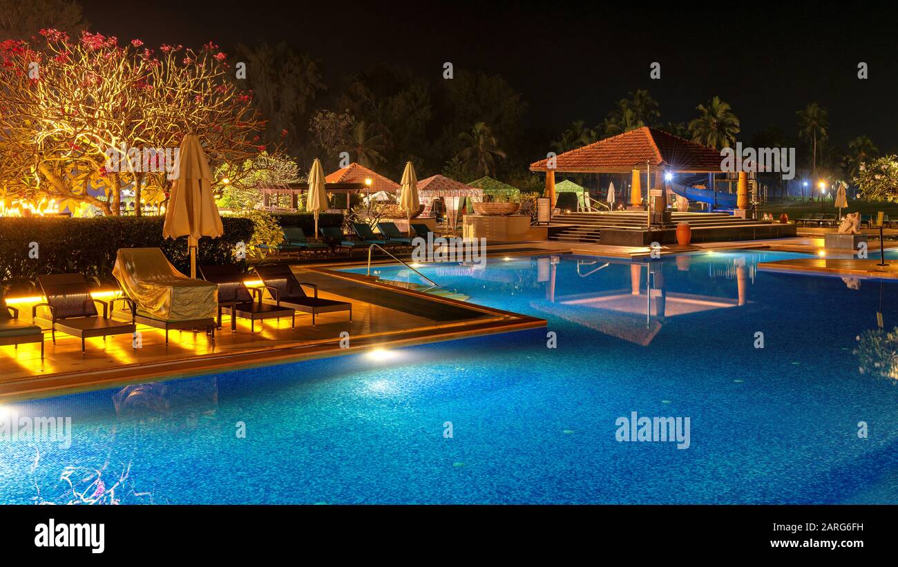 Night view of tropical pool surrounded by palm trees and lounge chairs ...