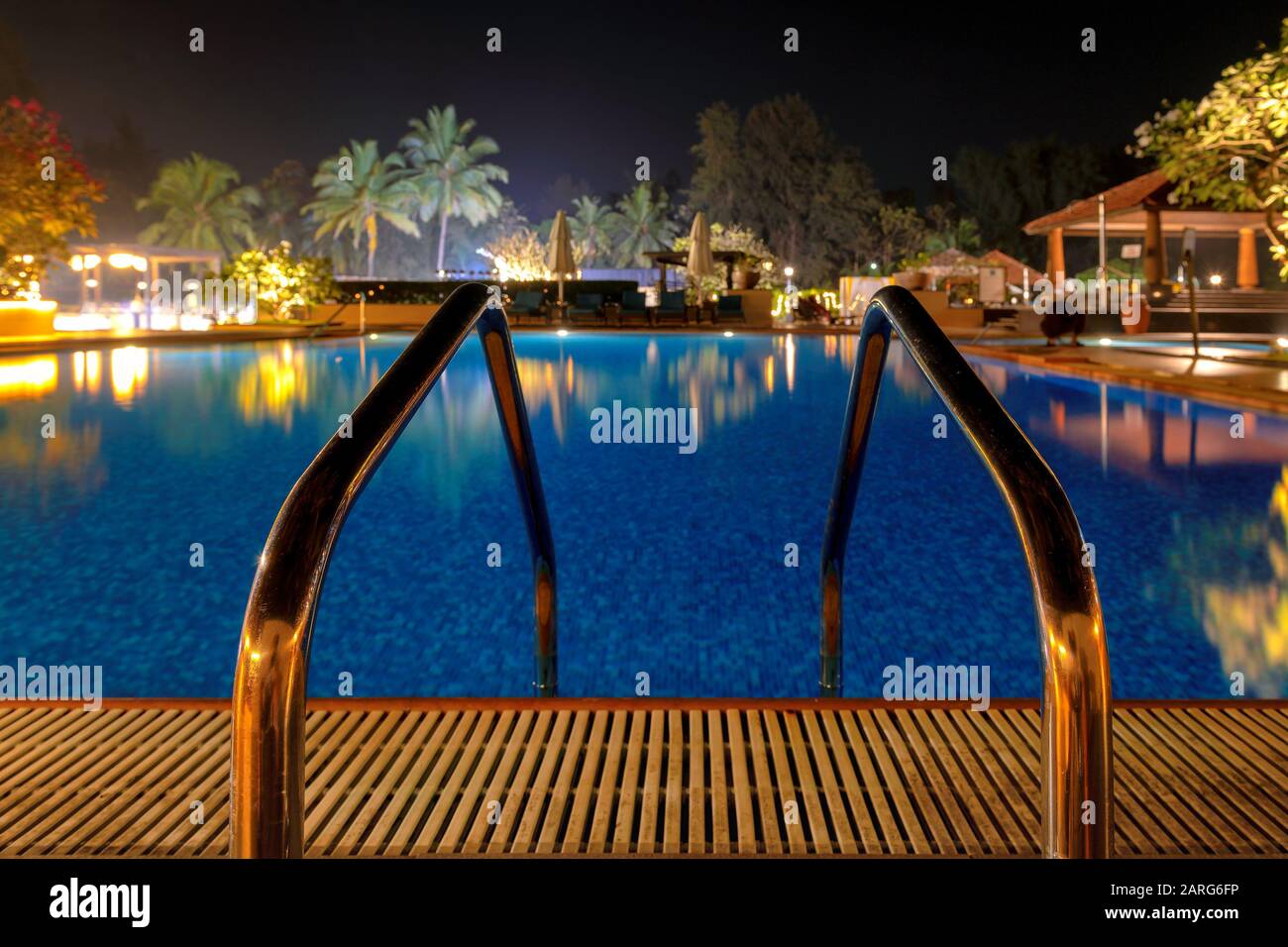 Night view of tropical pool surrounded by palm trees and lounge chairs ...