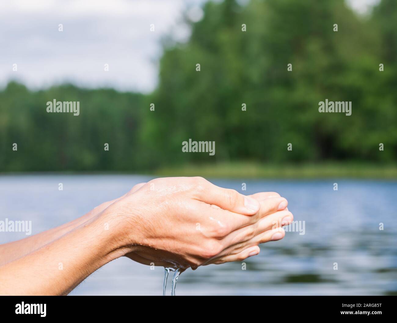 Woman taking raw unfiltered water from a natural source by a cupped ...