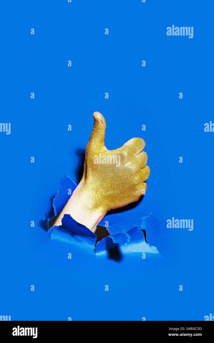 Hand with golden glitter break through the paper with the thumb up on ...