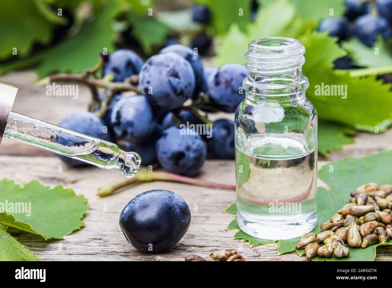 Grape seed oil in a glass jar and fresh grapes on old wooden boards ...