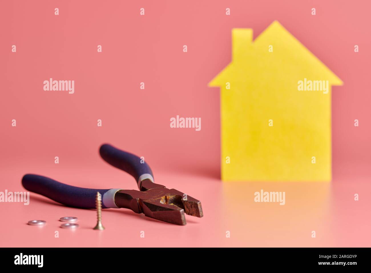 House renovation concept. Lineman pliers, screws and yellow house ...