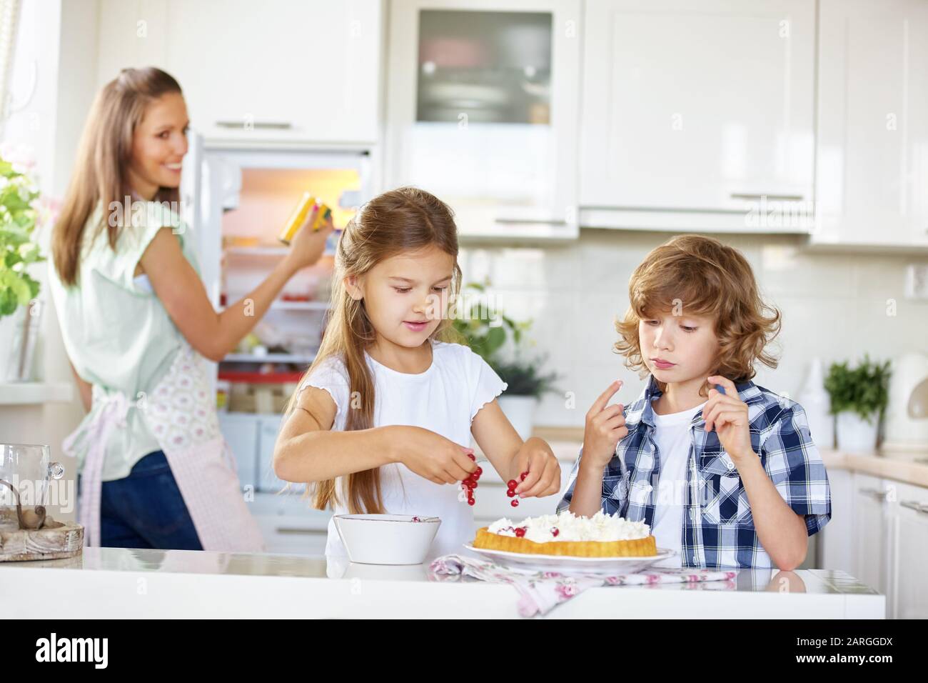 two children bake a cake together with their mother in the kitchen ...