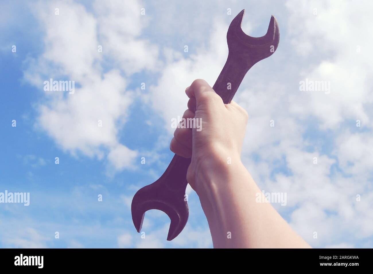 Hand holding up big wrench in the sky Stock Photo - Alamy