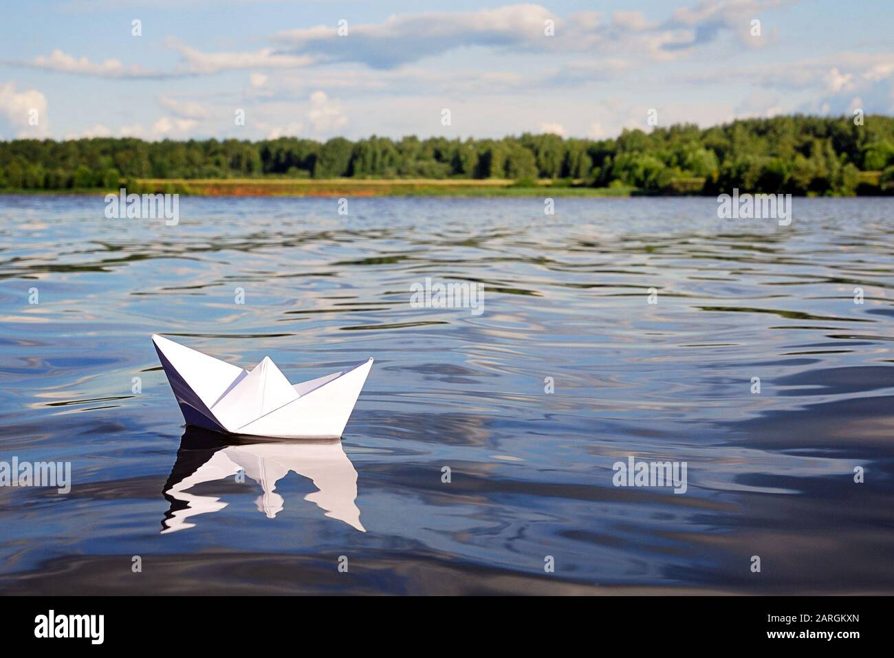 Small paper boat floating on blue calm river water, green forest, blue ...