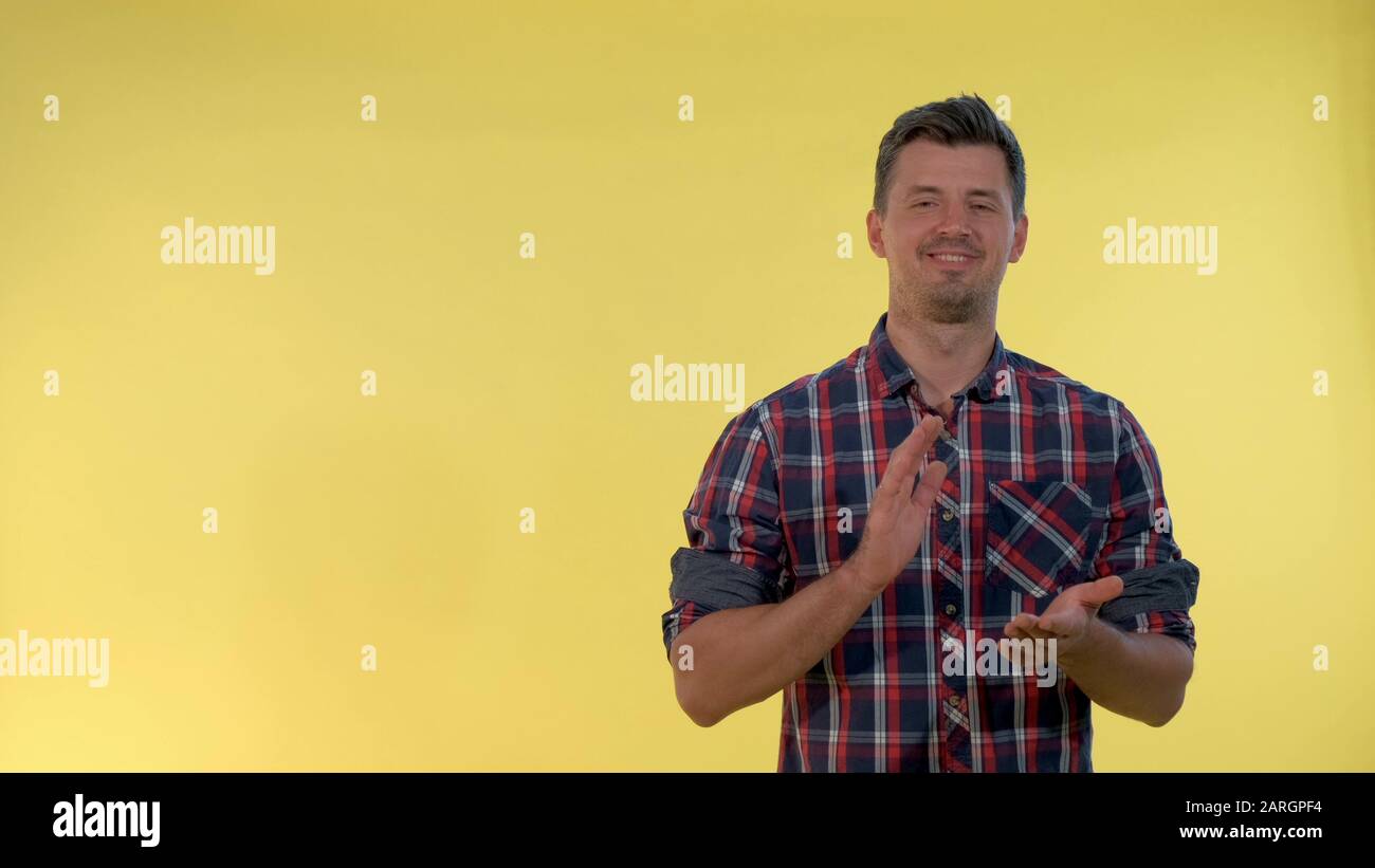 Portrait of smiling young man giving applause to somebody on yellow ...