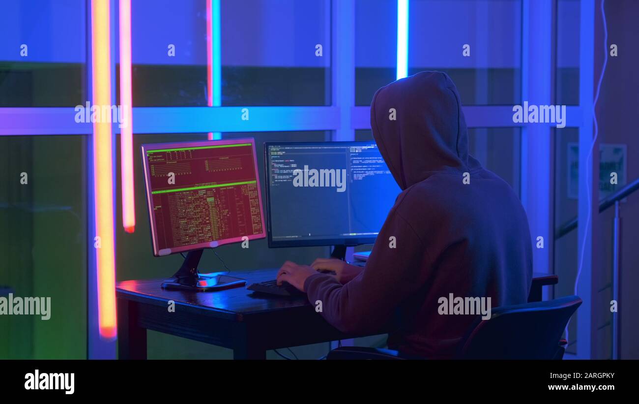 Back view of hacker dressed in a dark close working on computer. He ...