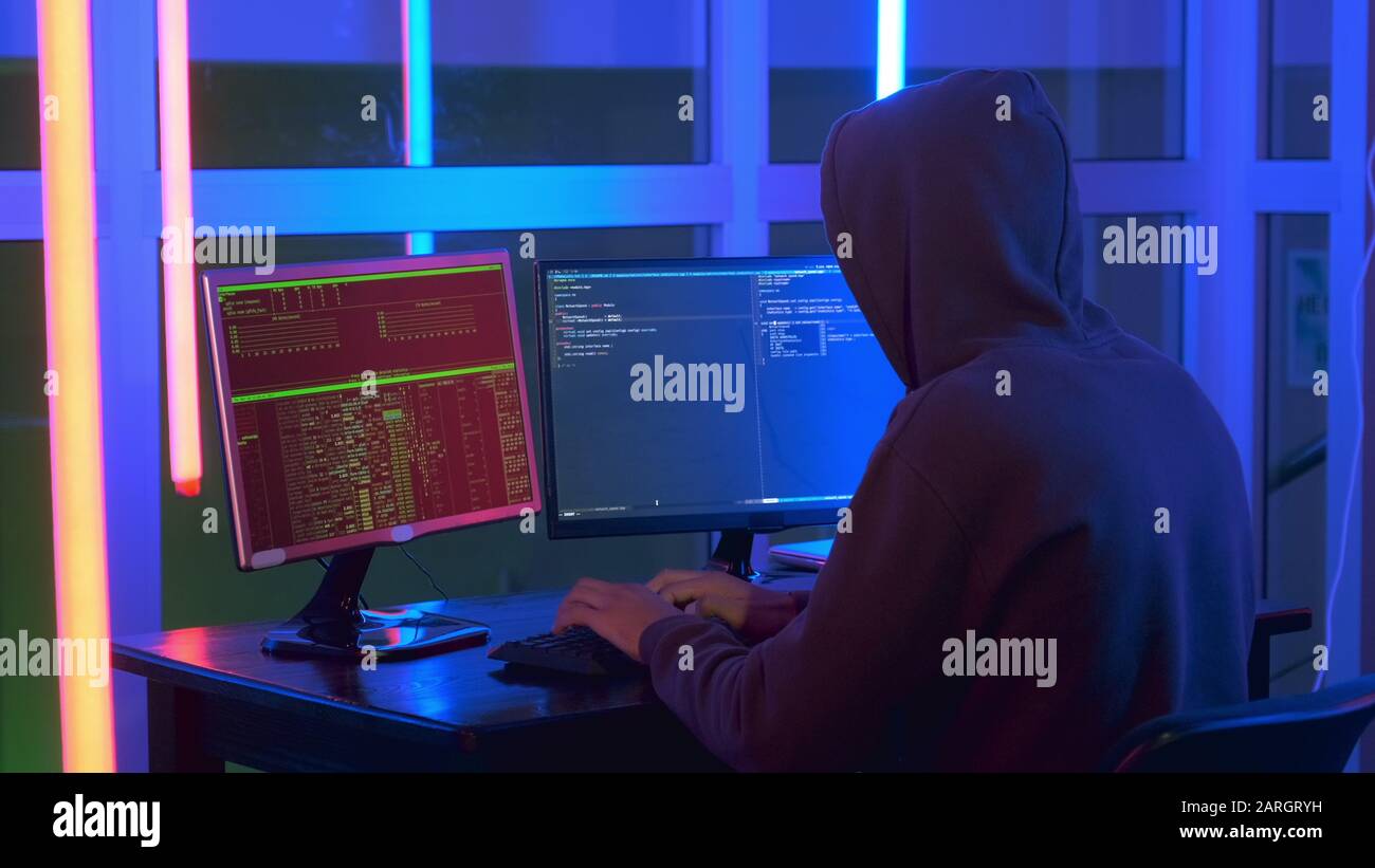 Medium shot of hacker dressed in a dark close working on computer. He ...