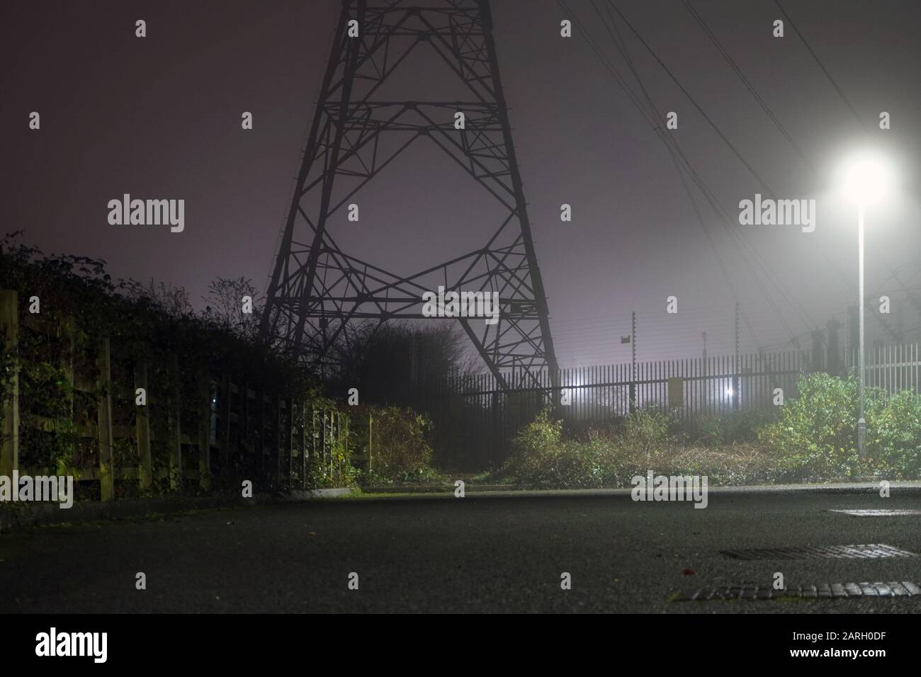 An electricity pylon on an industrial estate back lighted on a foggy ...