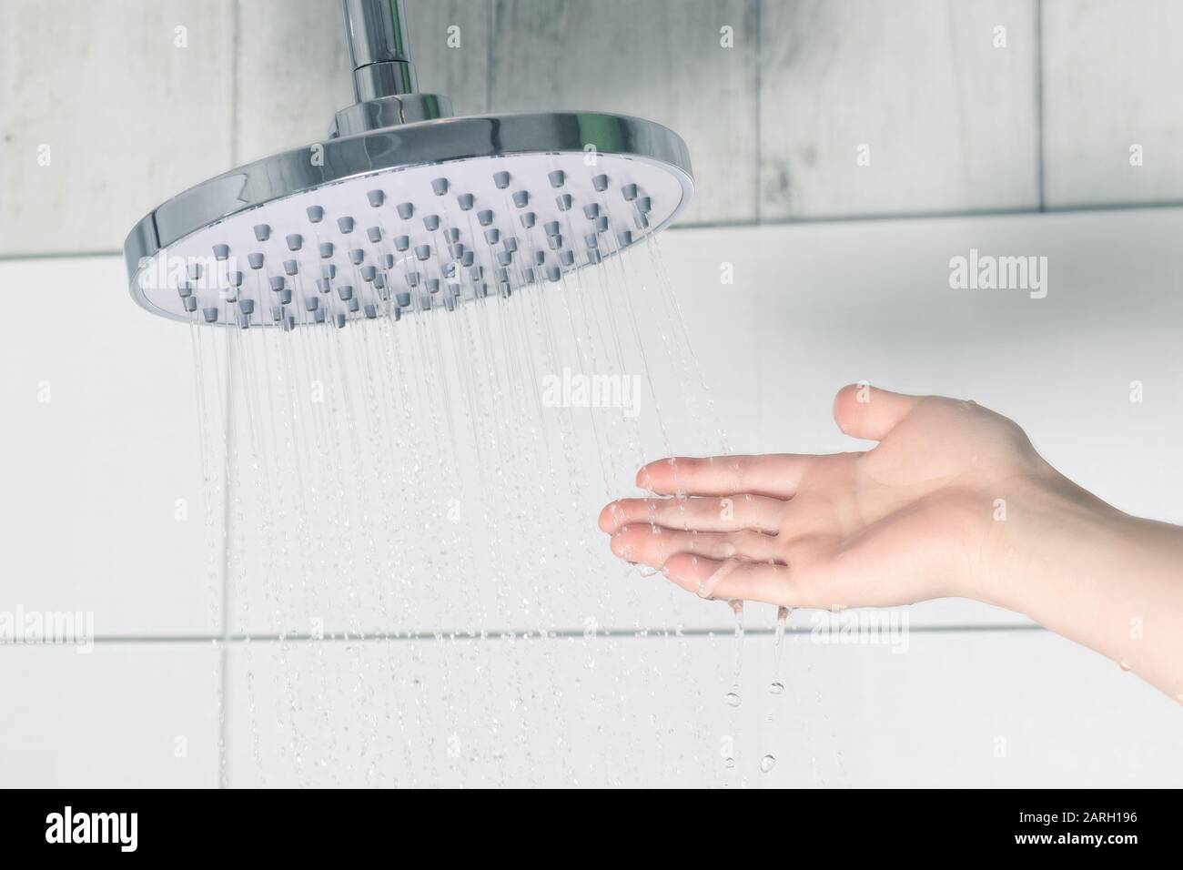 Female hand touching water pouring from a rain shower head, checking ...