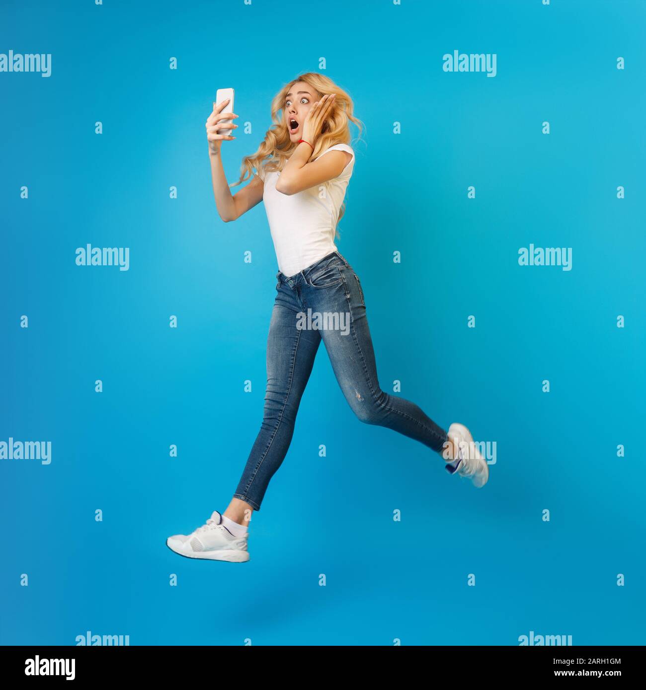 Shocked young woman jumping and using phone Stock Photo - Alamy