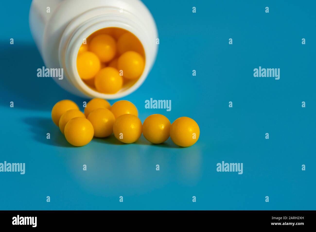 Yellow vitamins pour out from a pill bubble on a blue background ...