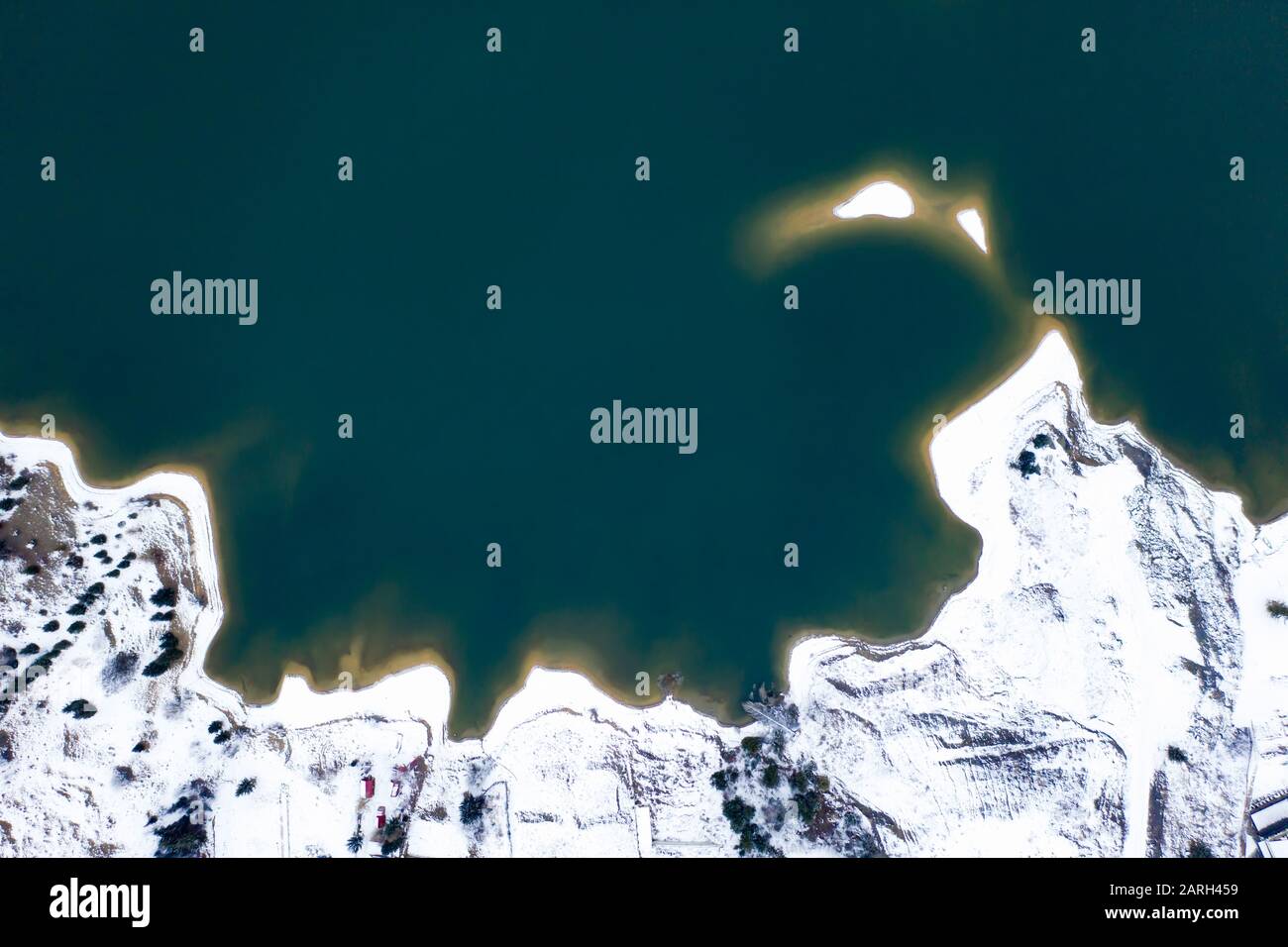 Aerial top view of snowy land and turquoise watered lake shore ...