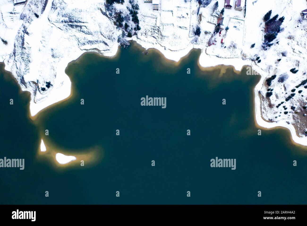 Aerial top view of snowy land and turquoise watered lake shore ...