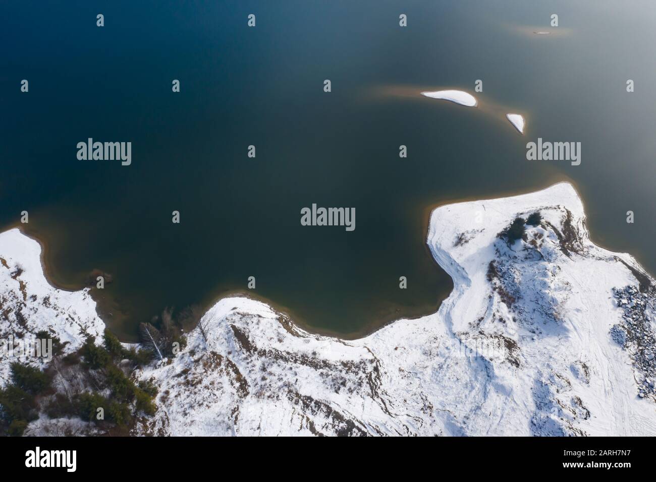 Aerial top view of snowy land and turquoise watered lake shore ...