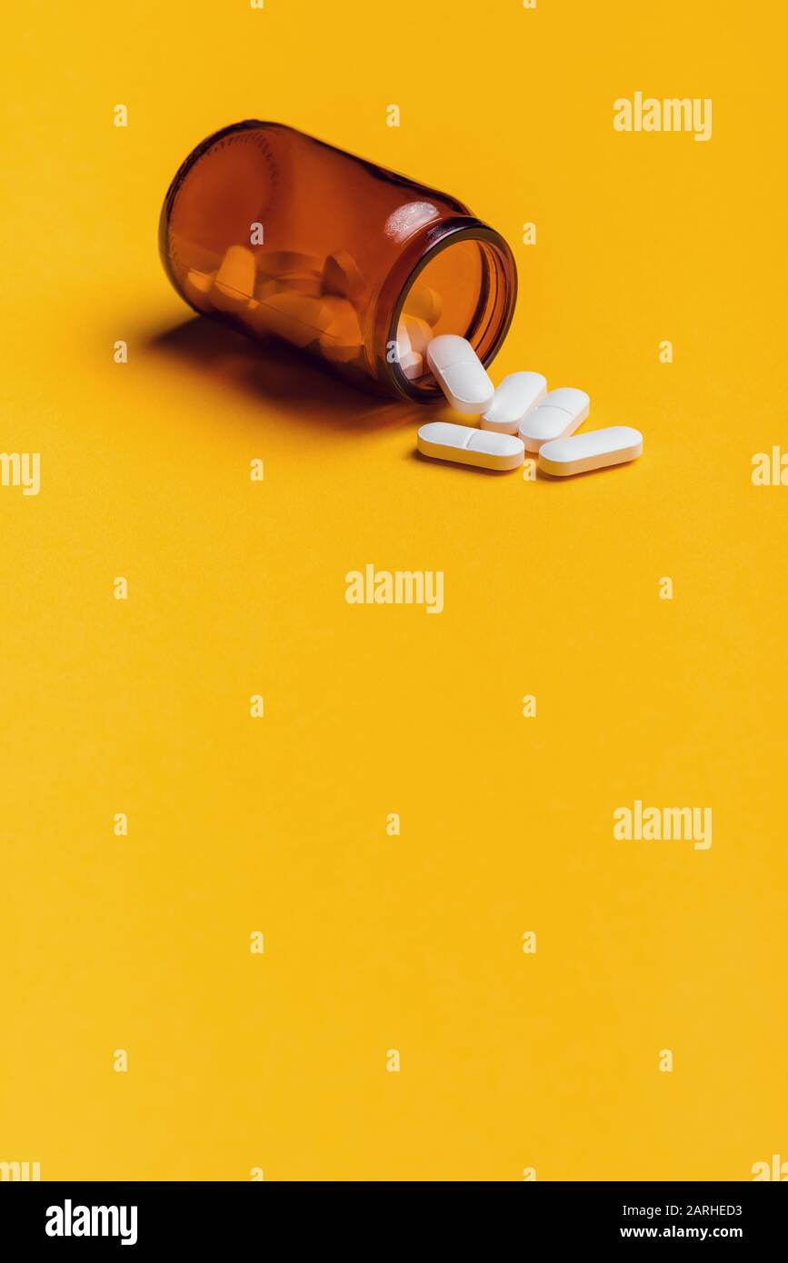 Film coated white oval pills spilled from bottle on yellow background ...