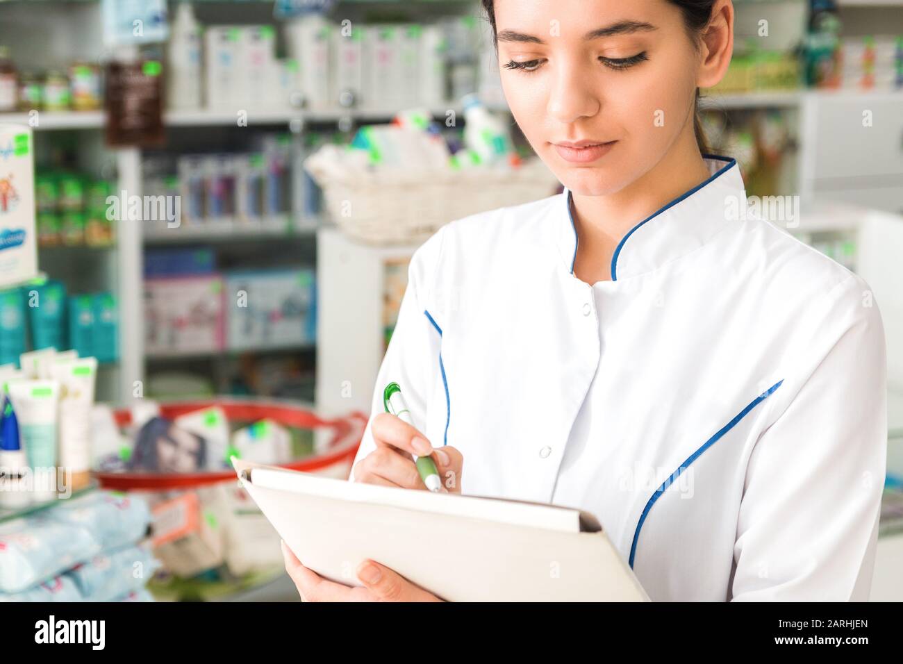 close up pharmacist with neutral emotions on face making notes in store ...