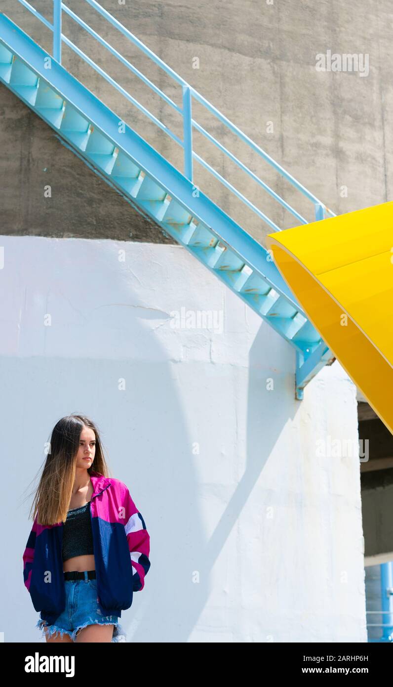 Trendy young woman stops while passing by industrial tanks and looks to ...