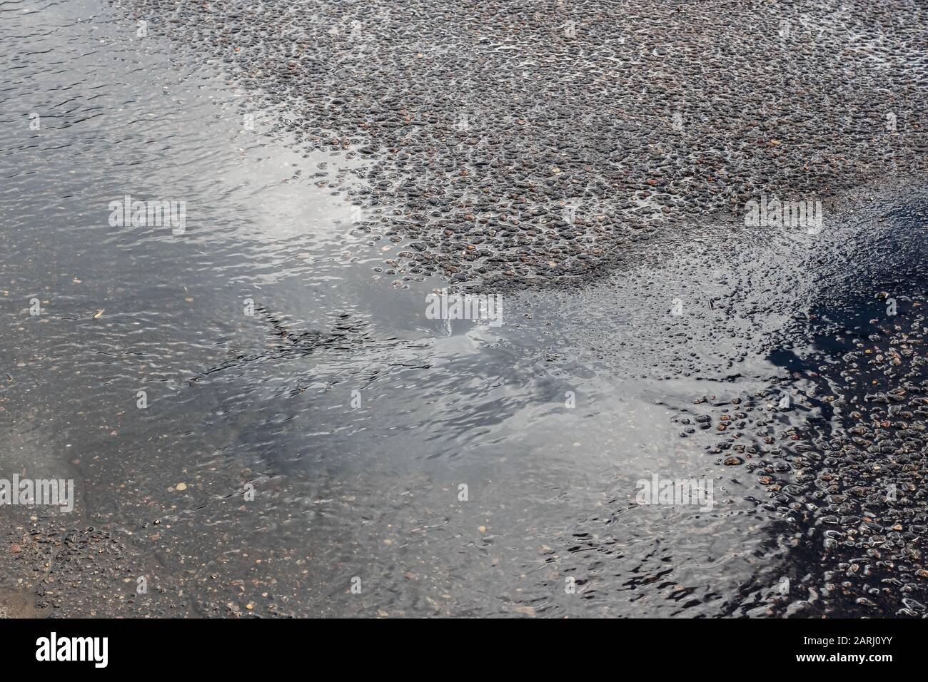 Water flows along the asphalt road close up, background or texture ...