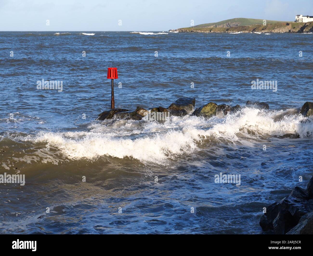 Waves breaking over rocks, red warning marker, Wales Stock Photo - Alamy