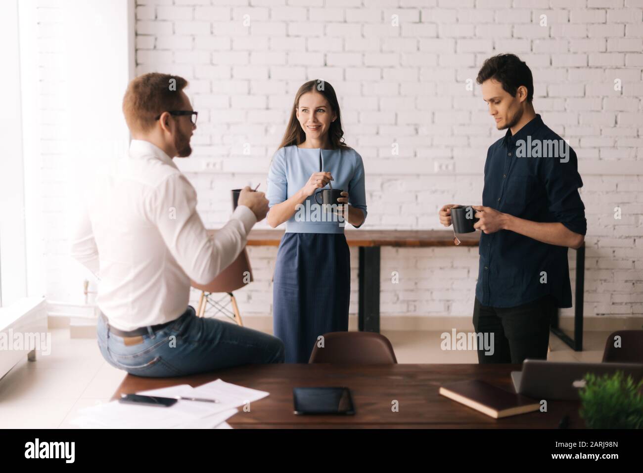 Three friendly coworkers standing in office, drinking coffee and ...