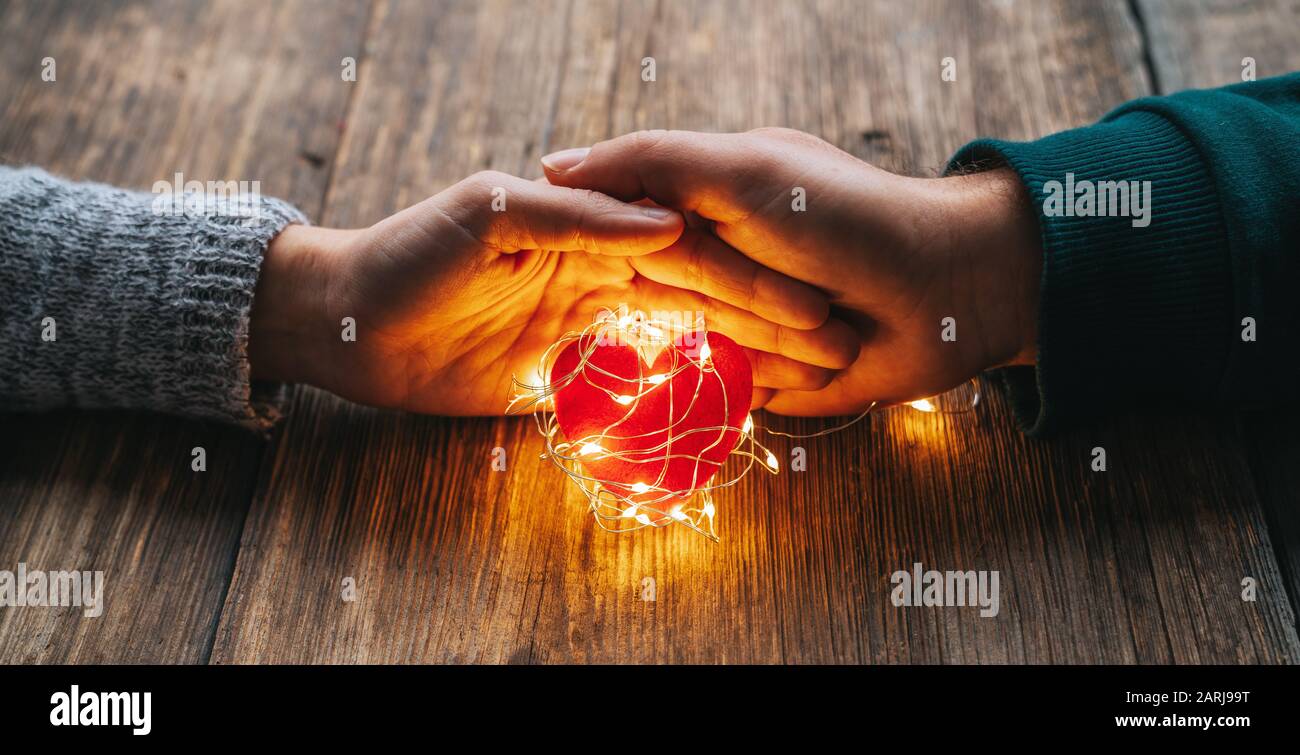 Two hands holding a red heart shape covered with led lights on wooden ...