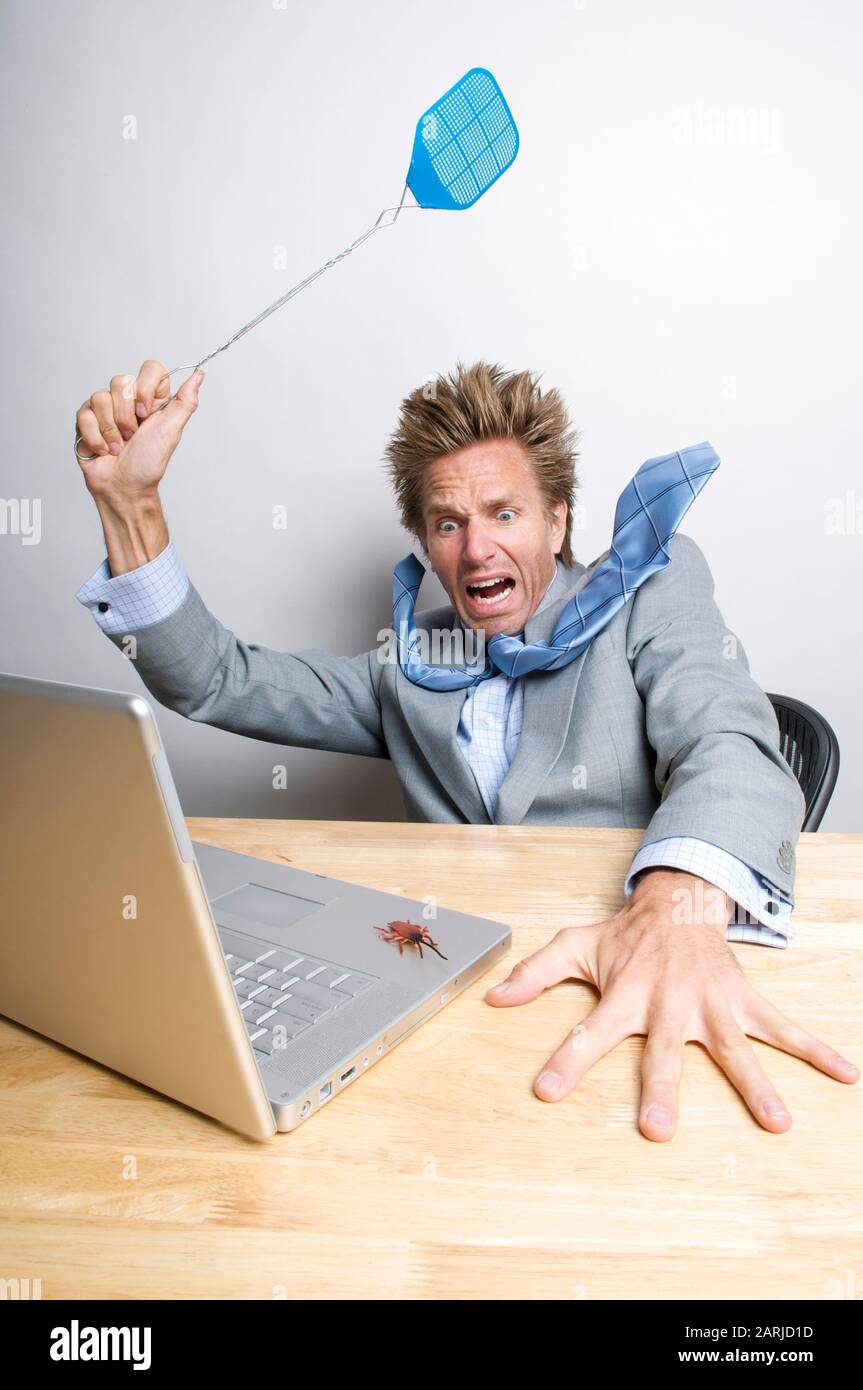Frightened businessman swatting a bug crawling on his laptop computer ...