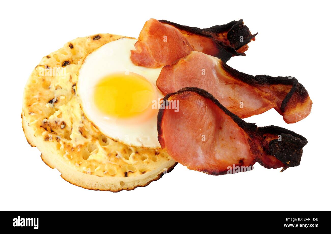 Fried egg and smoked bacon rashers on a large English crumpet isolated ...
