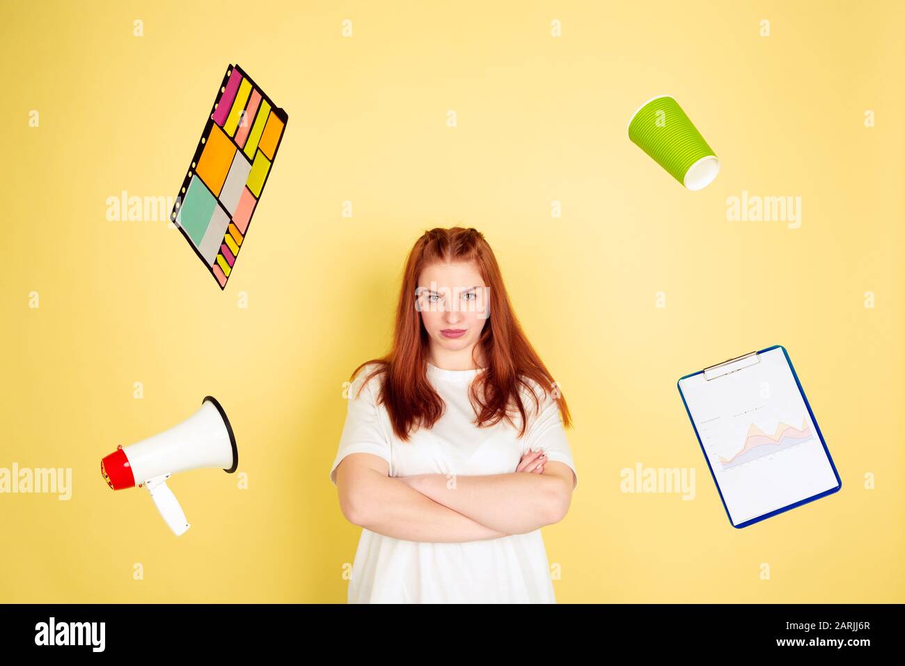 Angry, hands crossed. Caucasian young woman's portrait on yellow studio ...