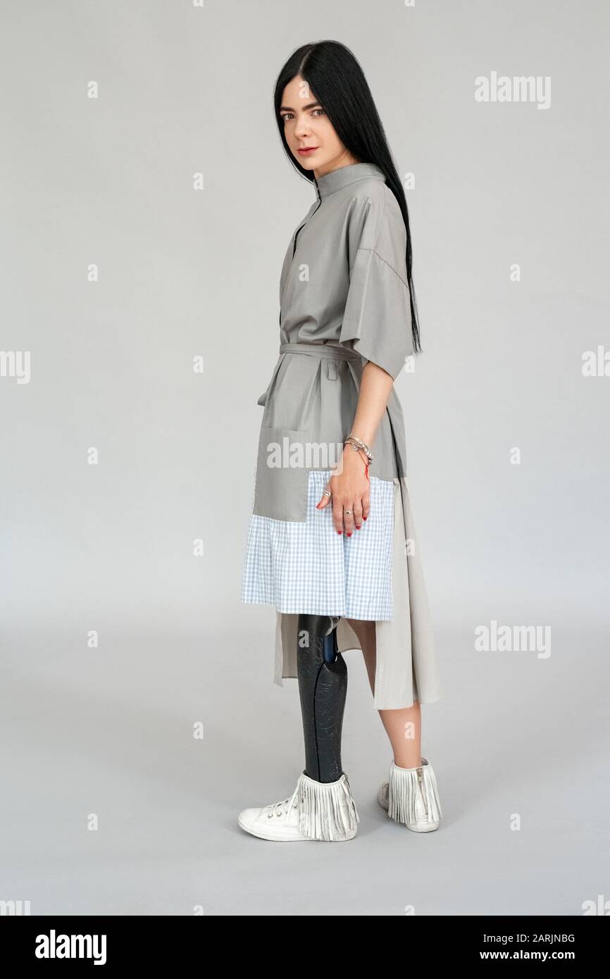 Freestyle. Diverse girl with leg prosthesis standing isolated on grey ...