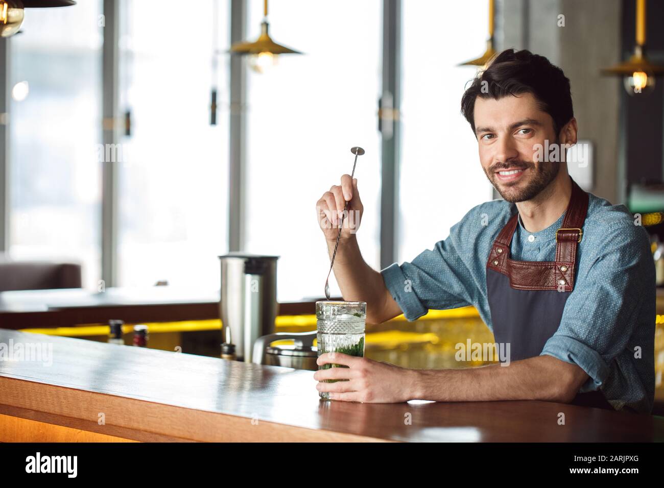 Making Drink. Bartender standing at counter mixing mojito smiling joyful Stock Photo - Alamy