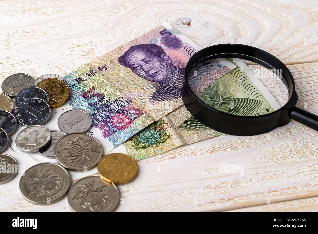 Magnifier on chinese yuan banknotes and coins on a white wooden surface ...