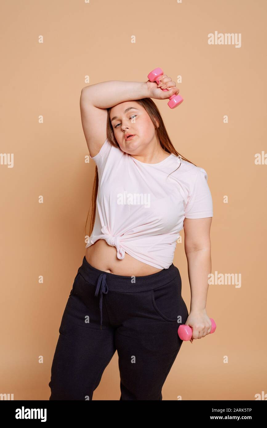 Very tired overweight woman with dumbbells on beige background Stock ...