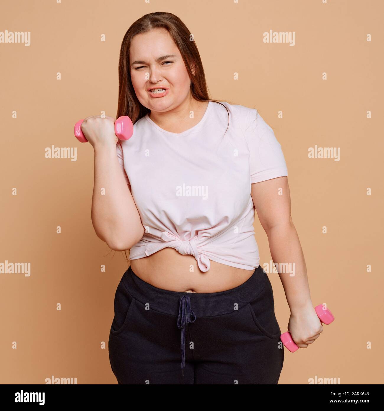 Overweight girl doing dumbbell exercises on beige background Stock ...