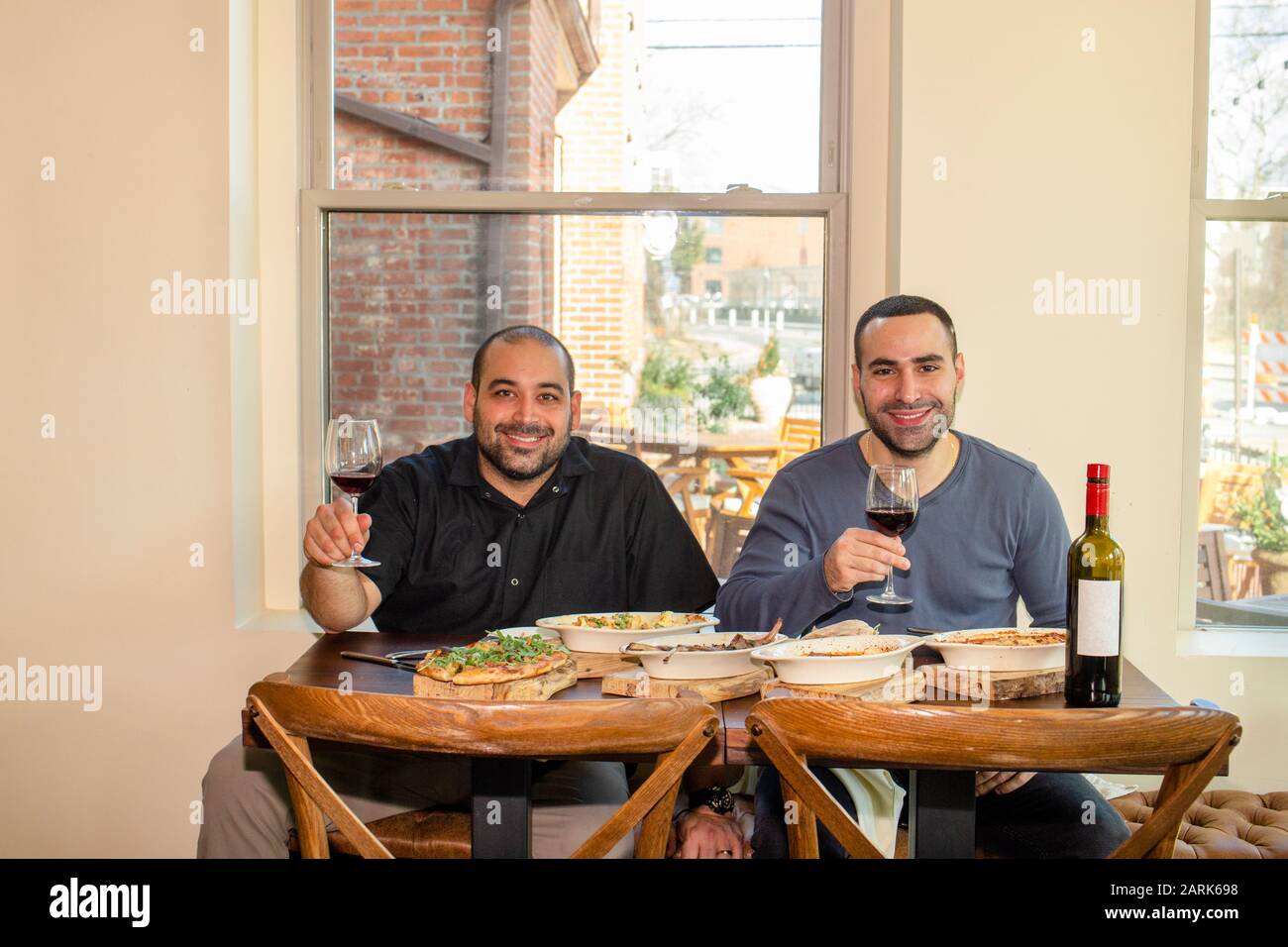 Two proud business owners sit together at a restaurant table with wine ...