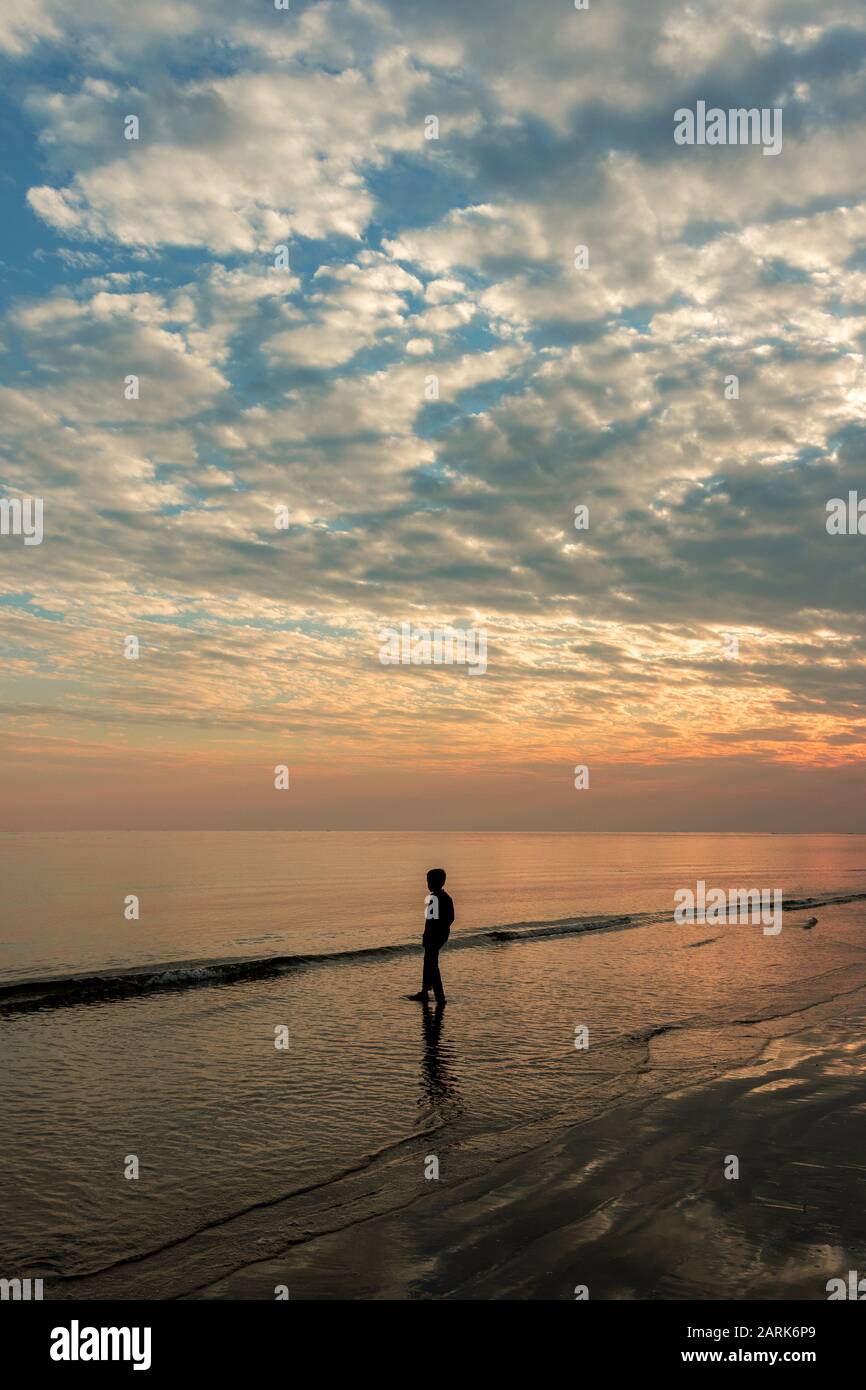 A boy standing on the beach witnessing the epic sunset Stock Photo - Alamy