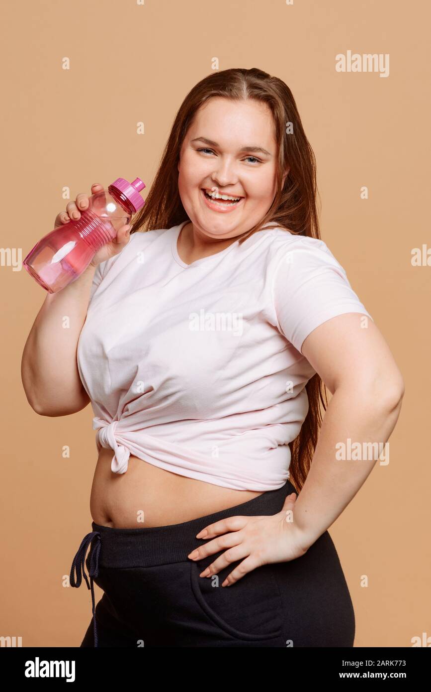 Overweight woman posing with bottle of water on beige background Stock ...
