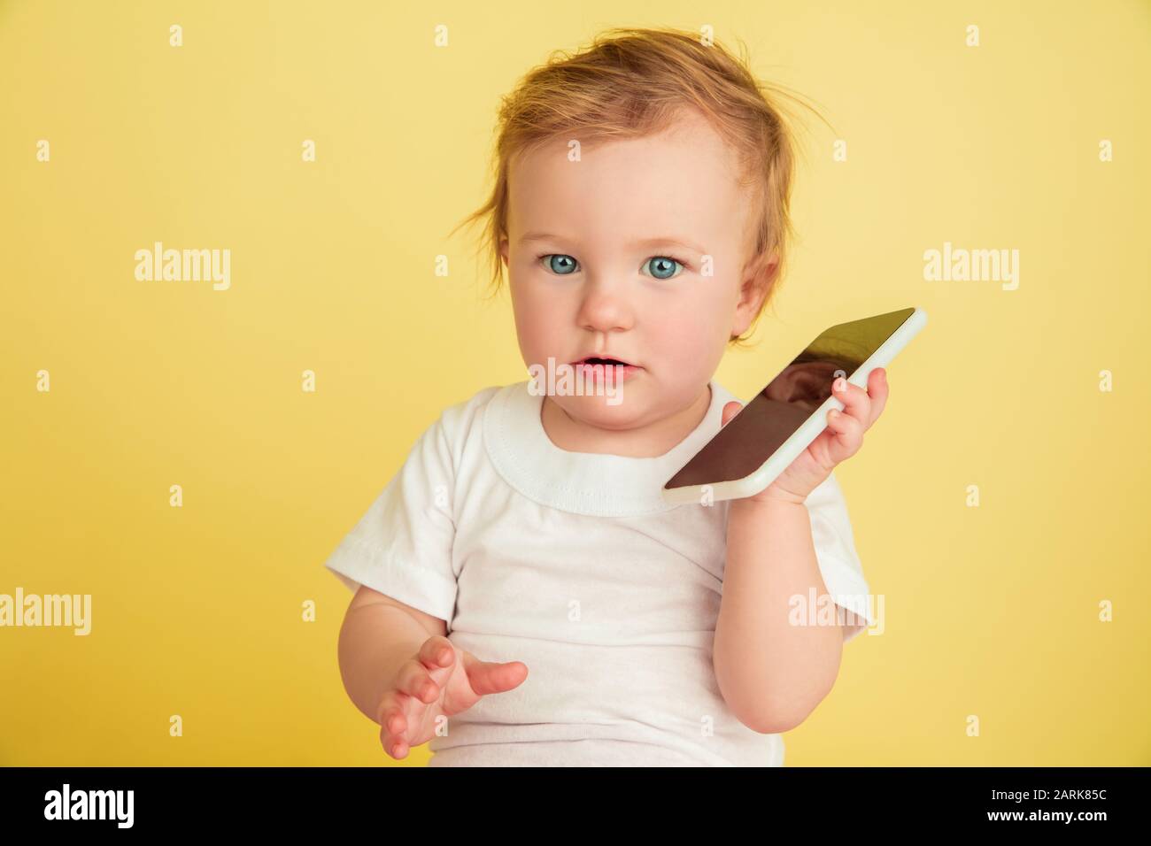 Calling mom. Caucasian little girl, children isolated on yellow studio ...