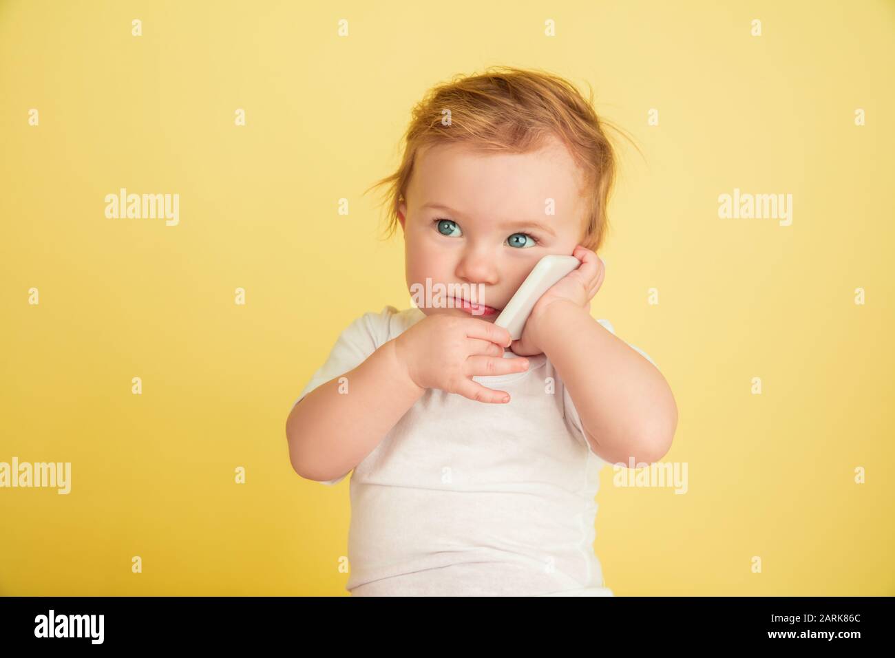 Calling mom. Caucasian little girl, children isolated on yellow studio ...