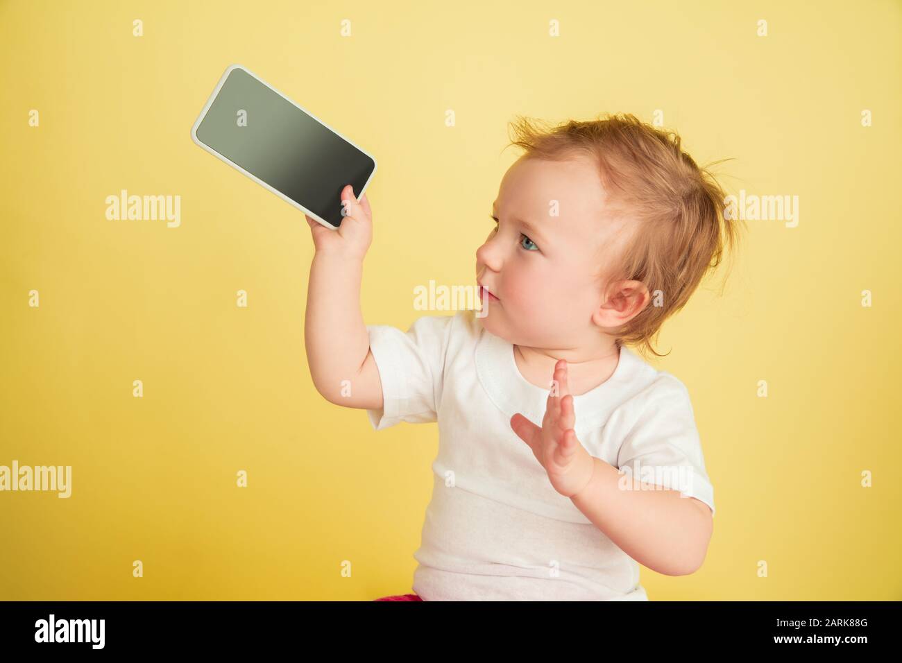 Calling mom. Caucasian little girl, children isolated on yellow studio ...