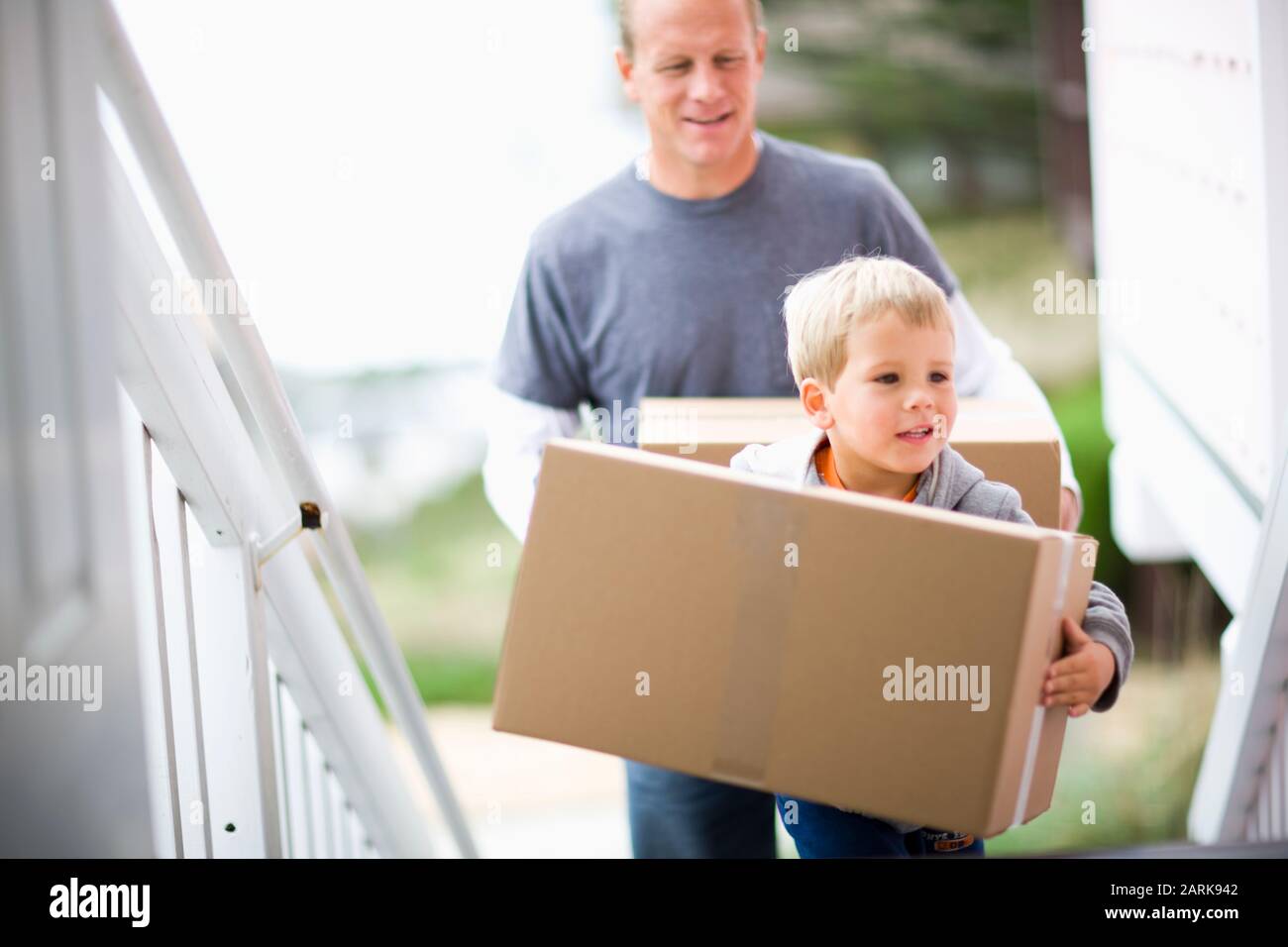 Young boy carrying boxes into a house with his mid-adult father Stock ...