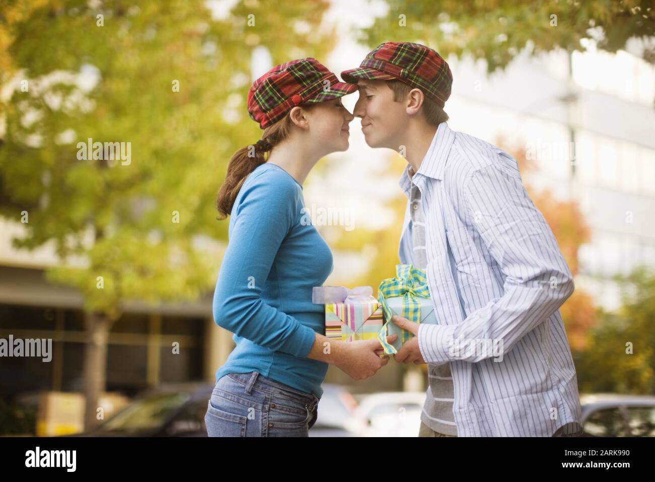 Young couple in matching plaid caps holding wrapped gifts while ...