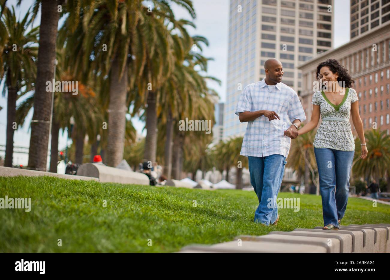 Happy Mid Adult Couple Holding Hands As They Walk Through A City Park