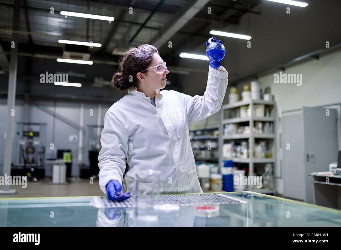 Laboratory woman in white lab coat with flask with blue liquid in her ...